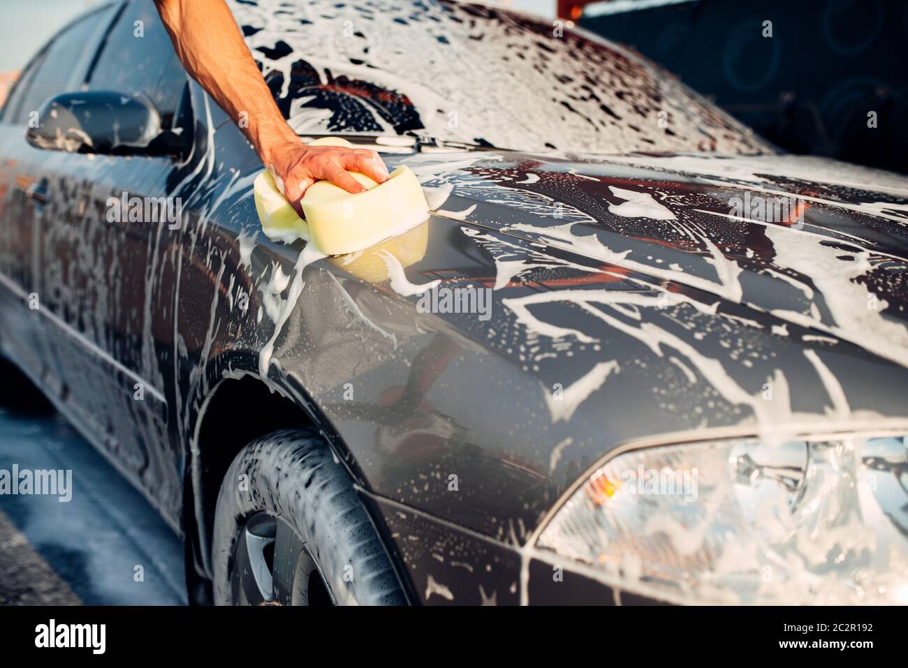Male hand rubbing the car with foam, automobile in suds. Carwash ...