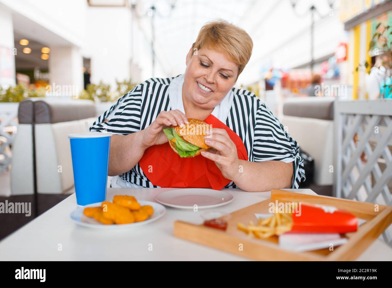 Fat woman eating fastfood in mall food court. Overweight female person ...