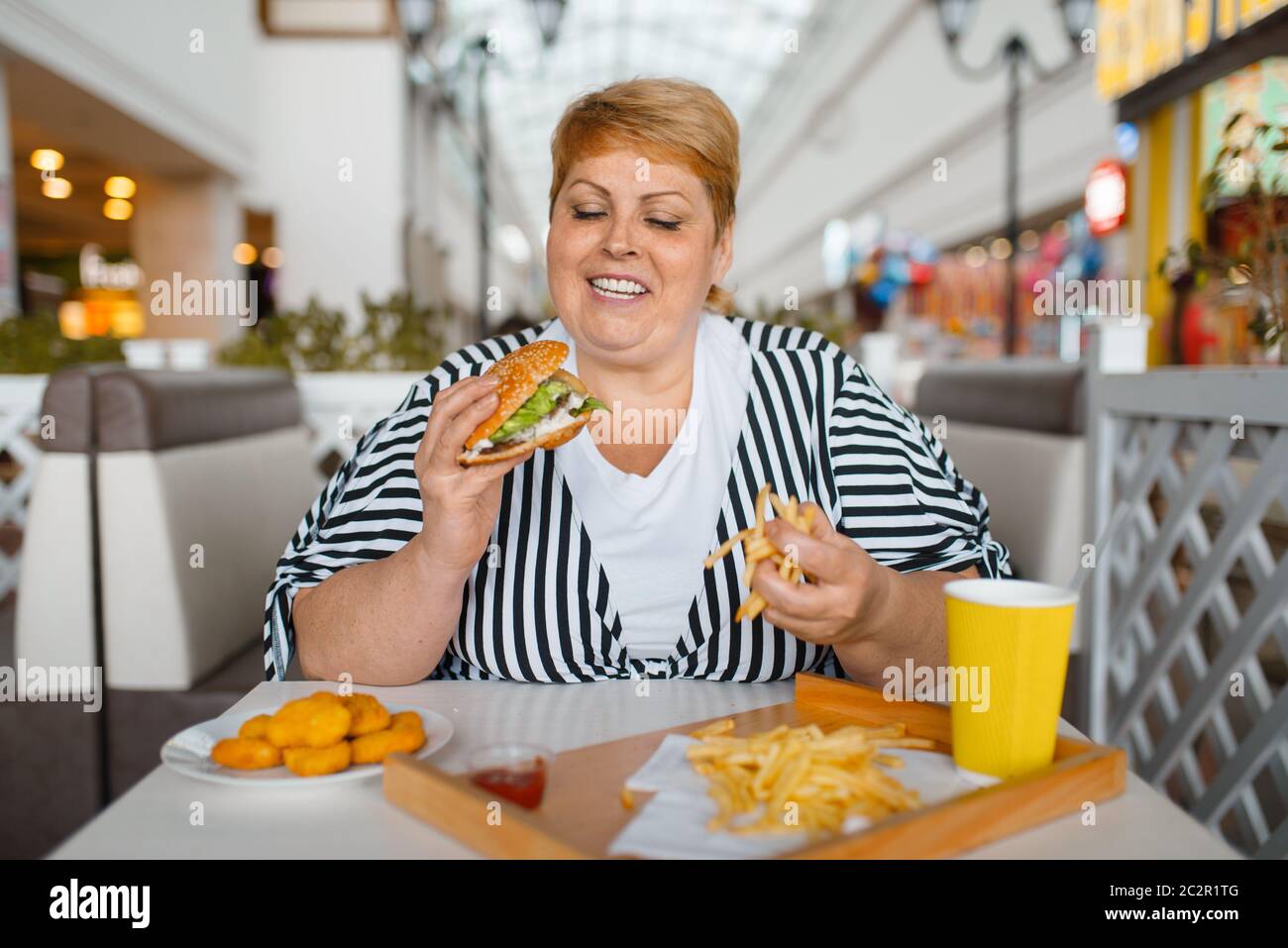 Fat woman eating high calorie food in fastfood restaurant. Overweight ...