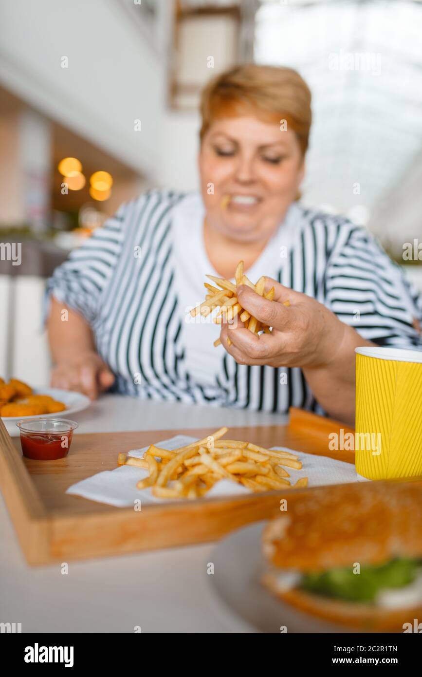 Fat woman eating high calorie food in mall restaurant. Overweight ...