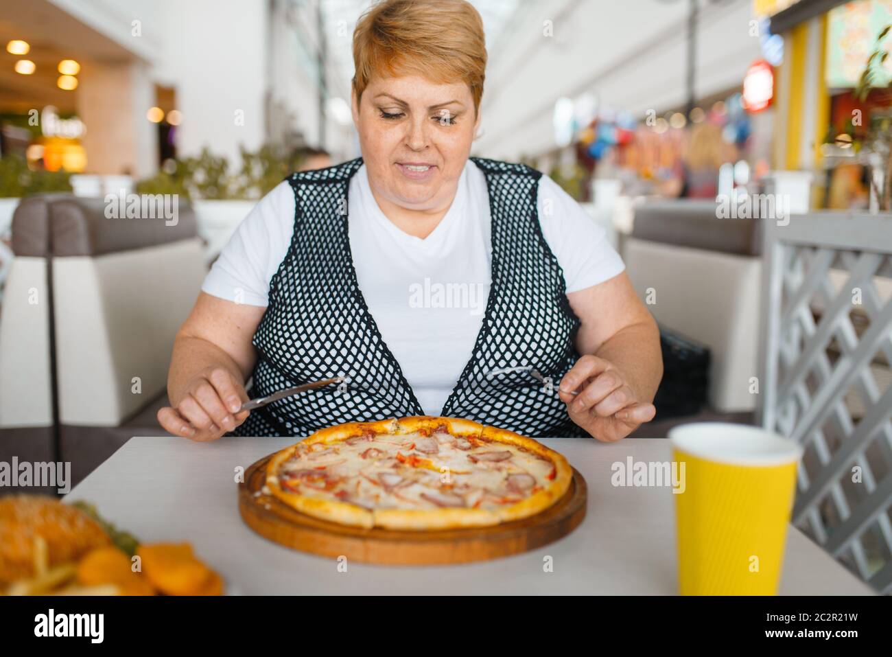 Fat woman eating pizza in fastfood restaurant. Overweight female person ...