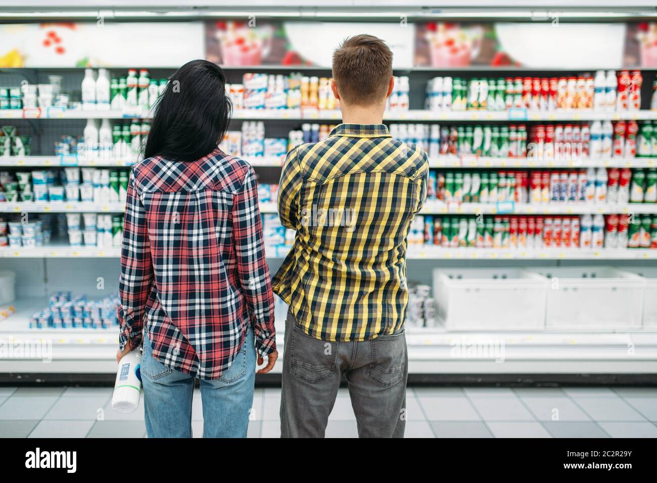 Young couple in supermarket, back view, milk department. Male and ...