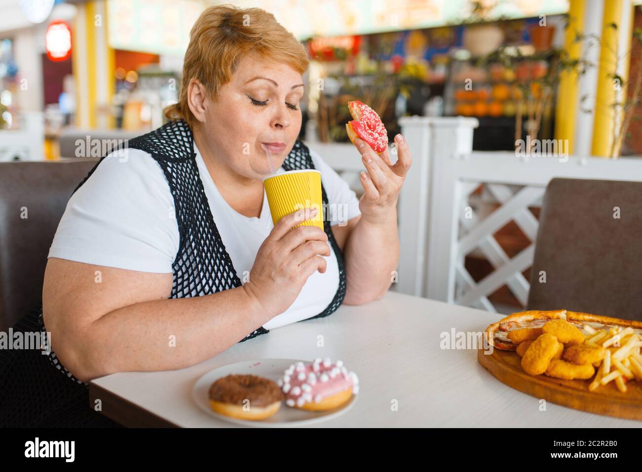 Fat woman eating doughnuts in fastfood restaurant, unhealthy food ...