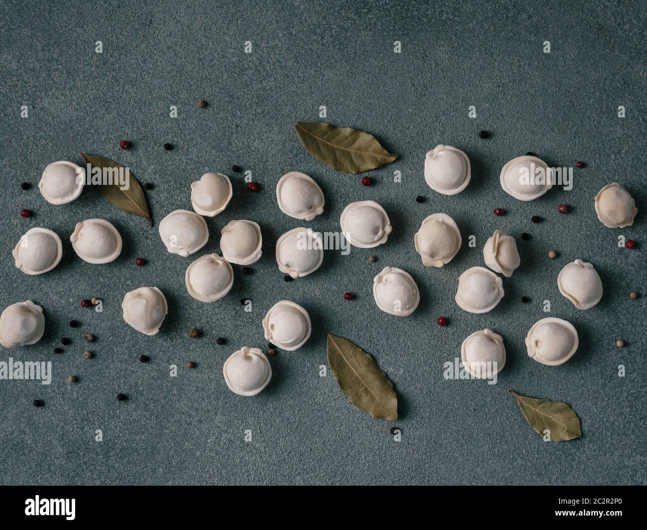 Pattern of frozen uncooked russian pelmeni with peppercorns and bay ...