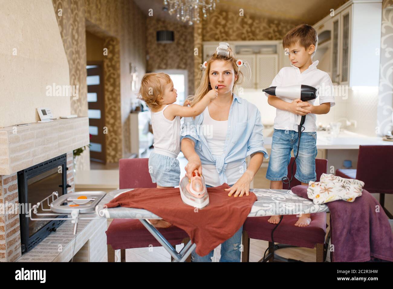 Housewife and kids playing with hair dryer at the ironing board. Woman ...