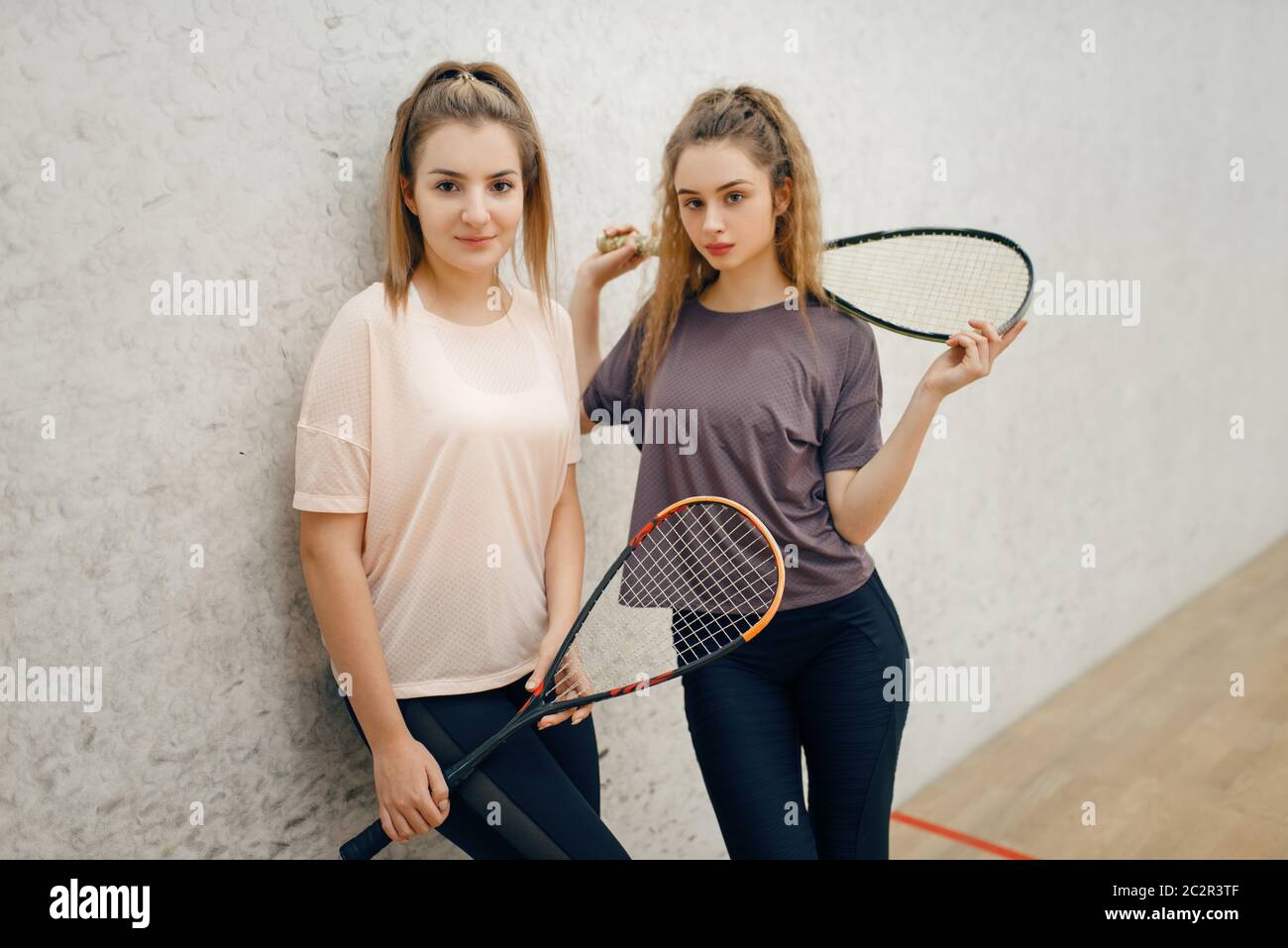 Two female players poses with squash rackets on court. Girls on game ...