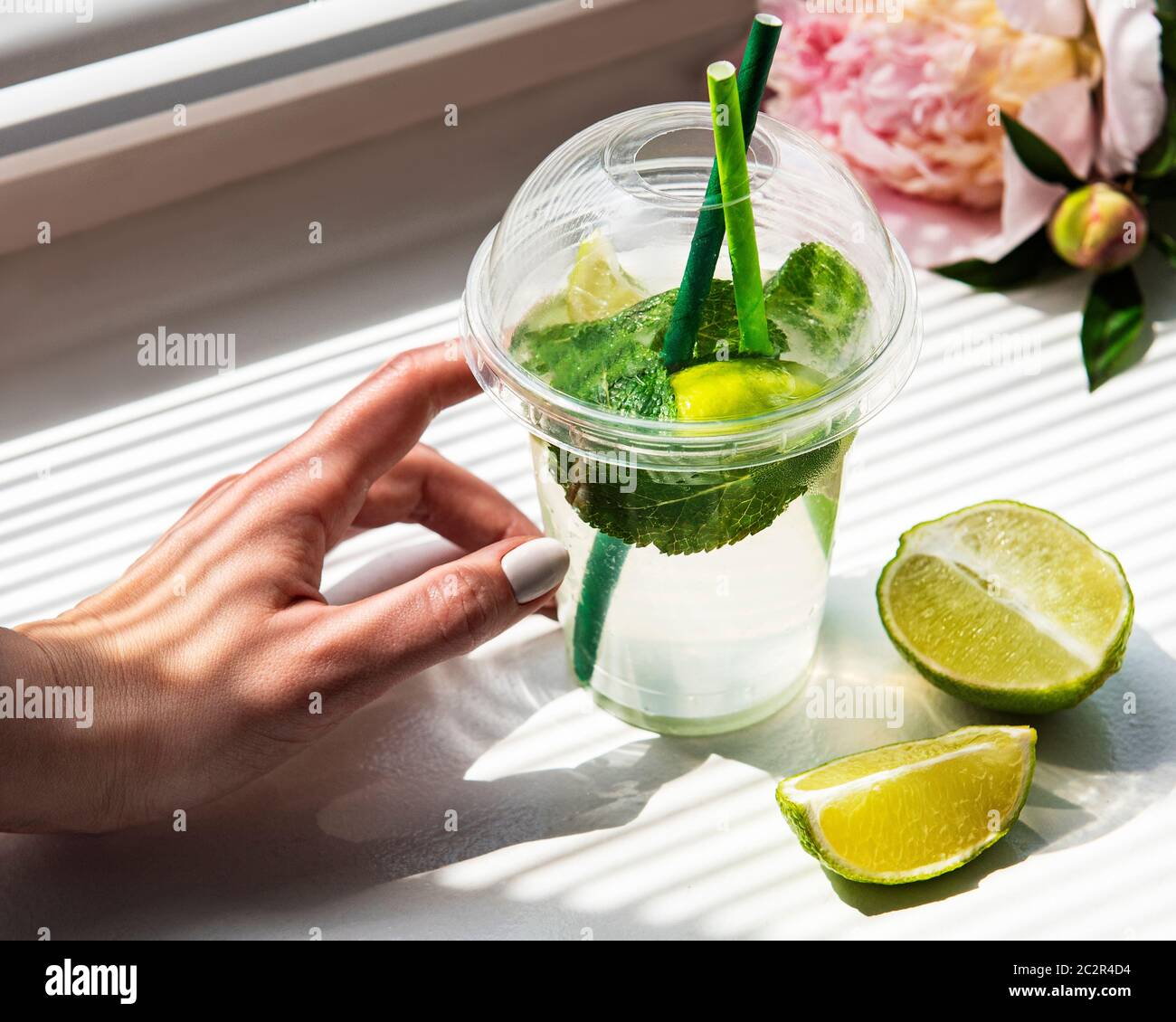 Mojito cocktail in female hands in front of the window and a bouquet of ...