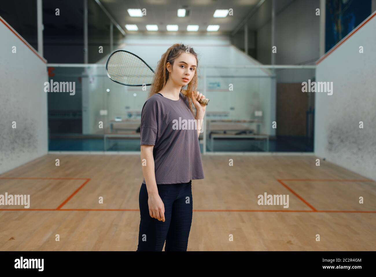 Female player poses with squash racket on court. Girl on game training ...