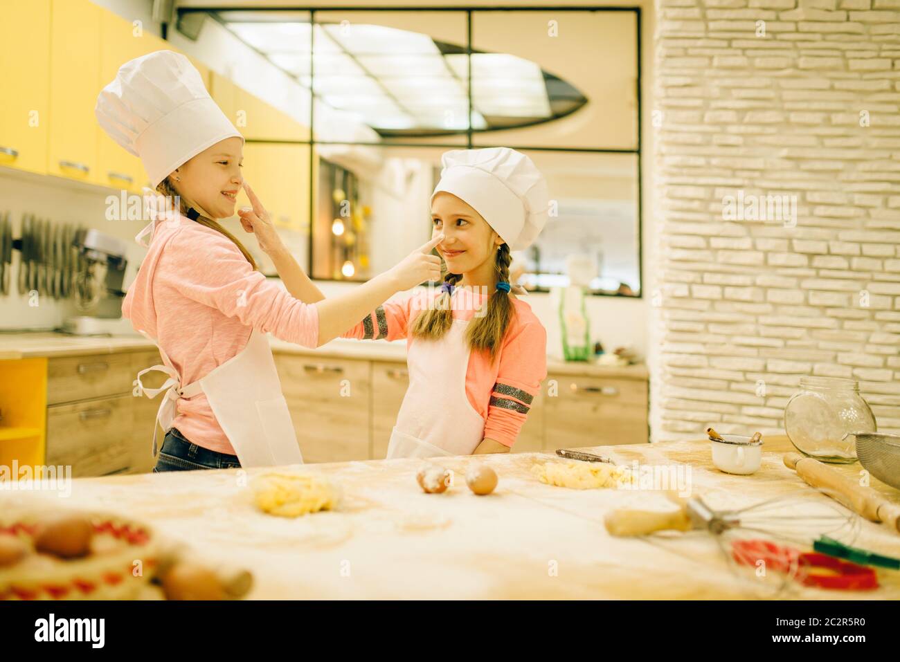 Two smiling little girls cooks in caps and aprons having fun, cookies ...