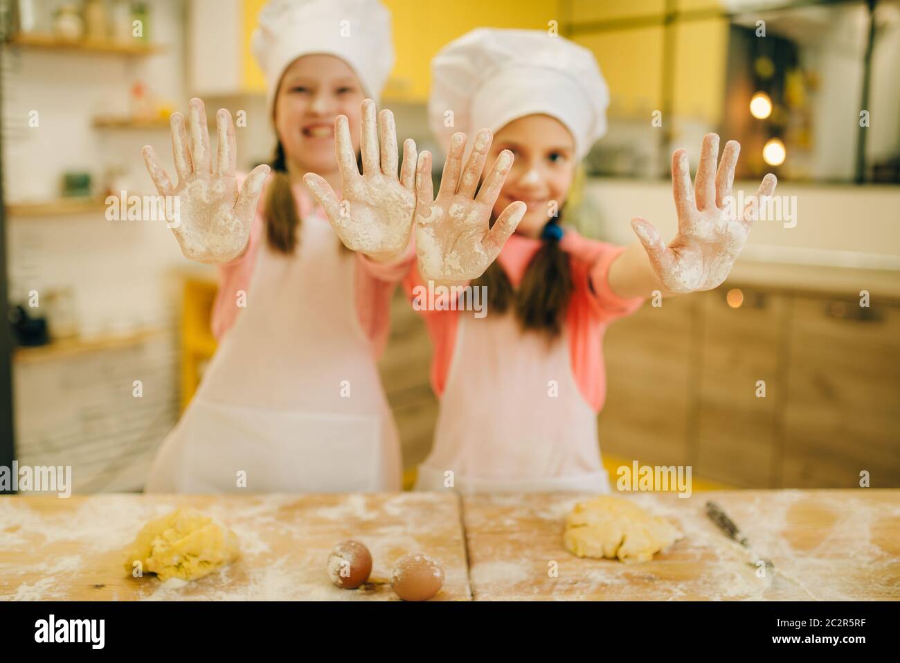 Two little girls cooks in caps shows hands covered in flour, cookies ...