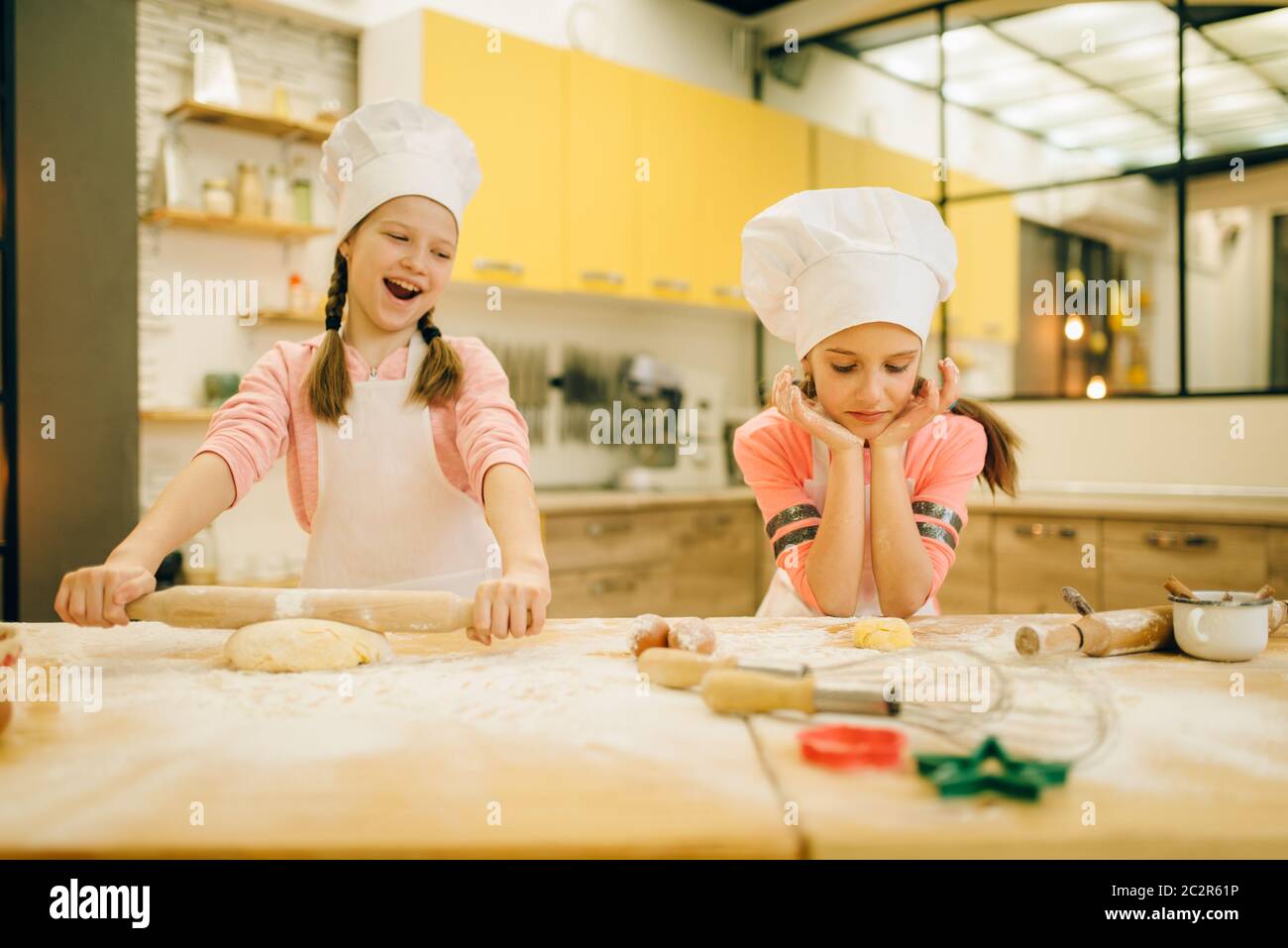 Two little girls chefs are laughing at each other, cookies preparation ...