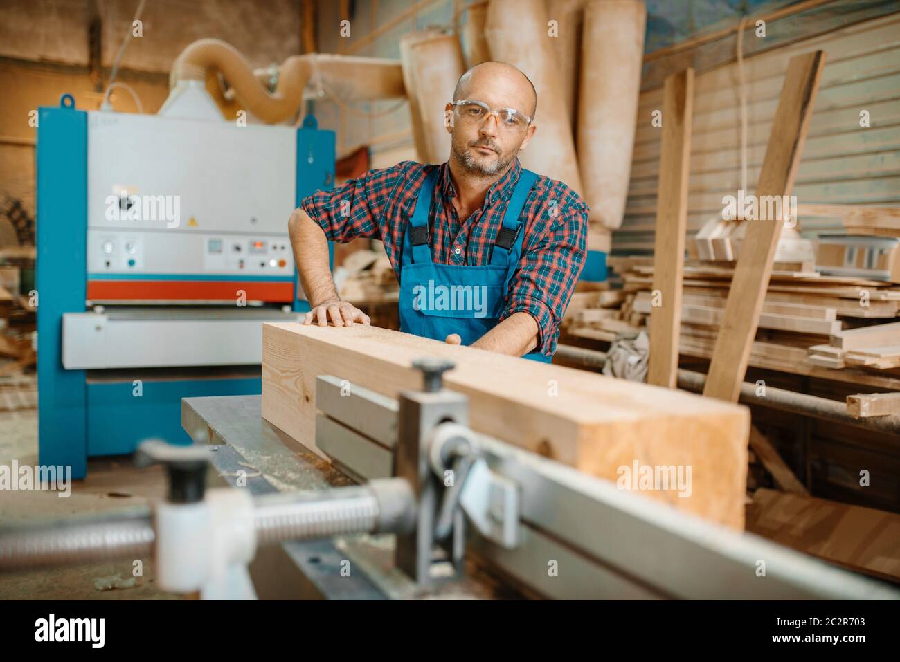 Carpenter processes wooden beam on plane machine, woodworking, lumber ...