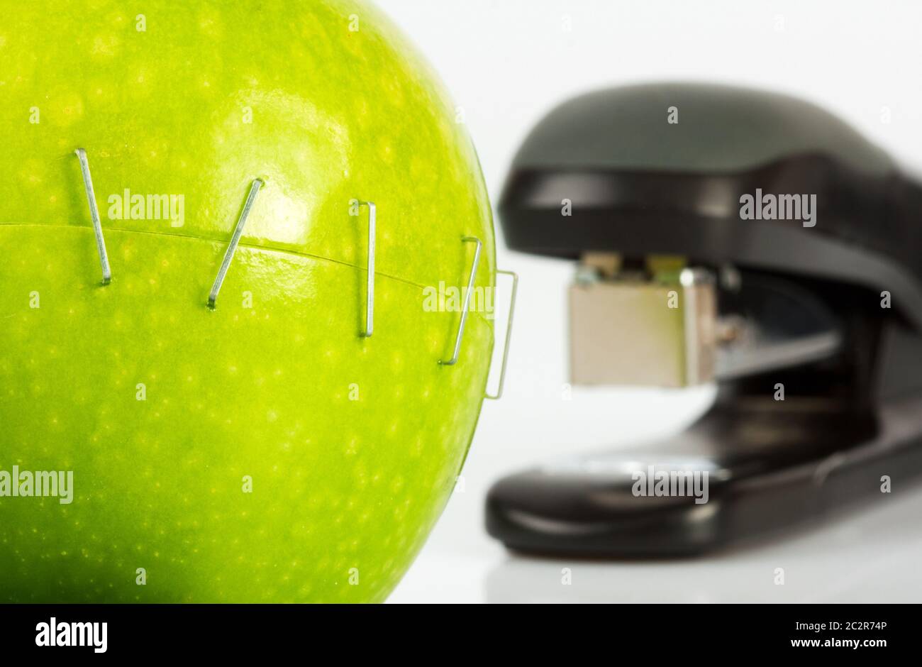 Two parts of green apple stapled together and stapler on background ...