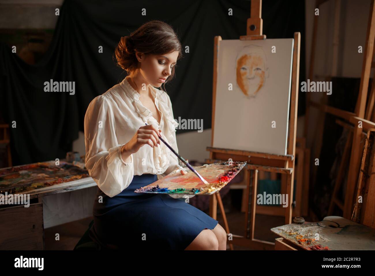 Female painter holds color palette and brush in studio. Creative ...