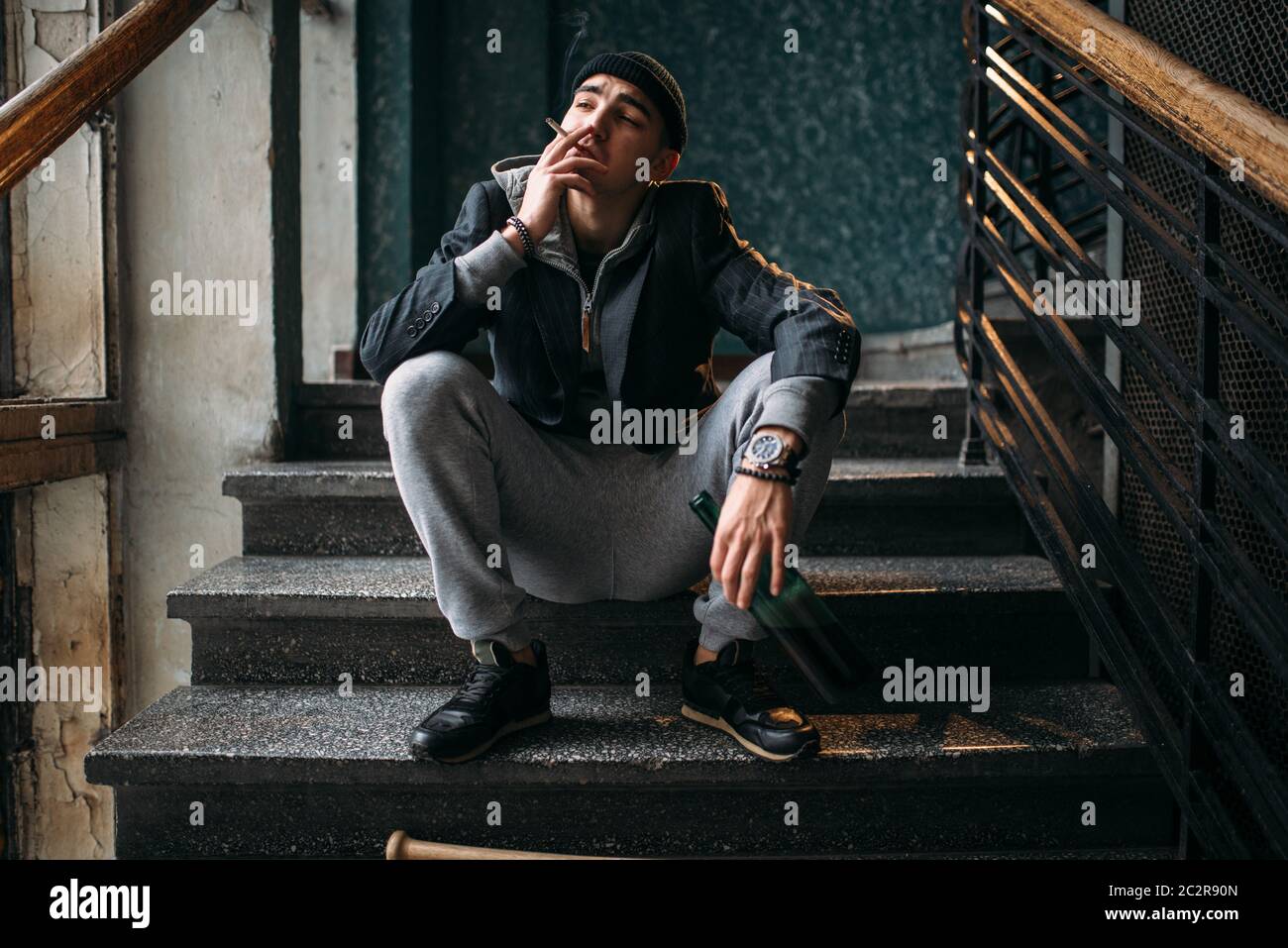 Bad guy with bottle of beer sits on the stairs and smoking. Street ...