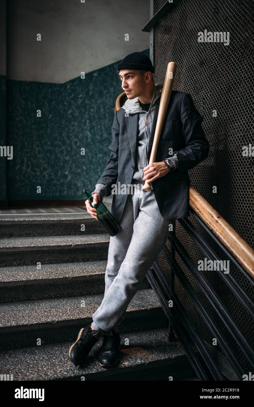 Bad guy with baseball bat and bottle of beer standing on the stairs ...