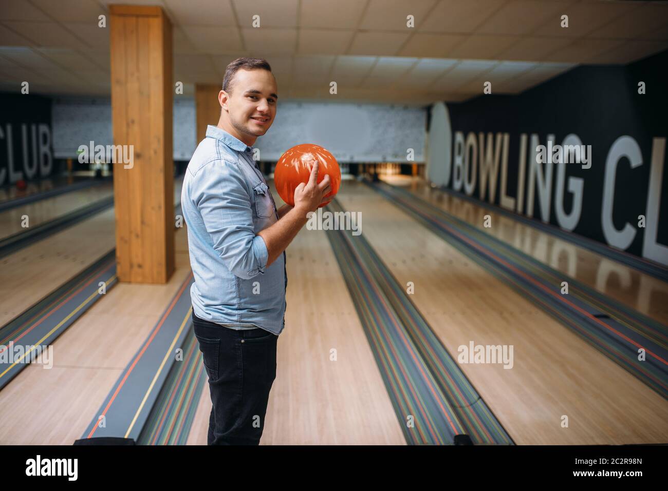 Male bowler standing on lane and poses with ball in hands, back view ...