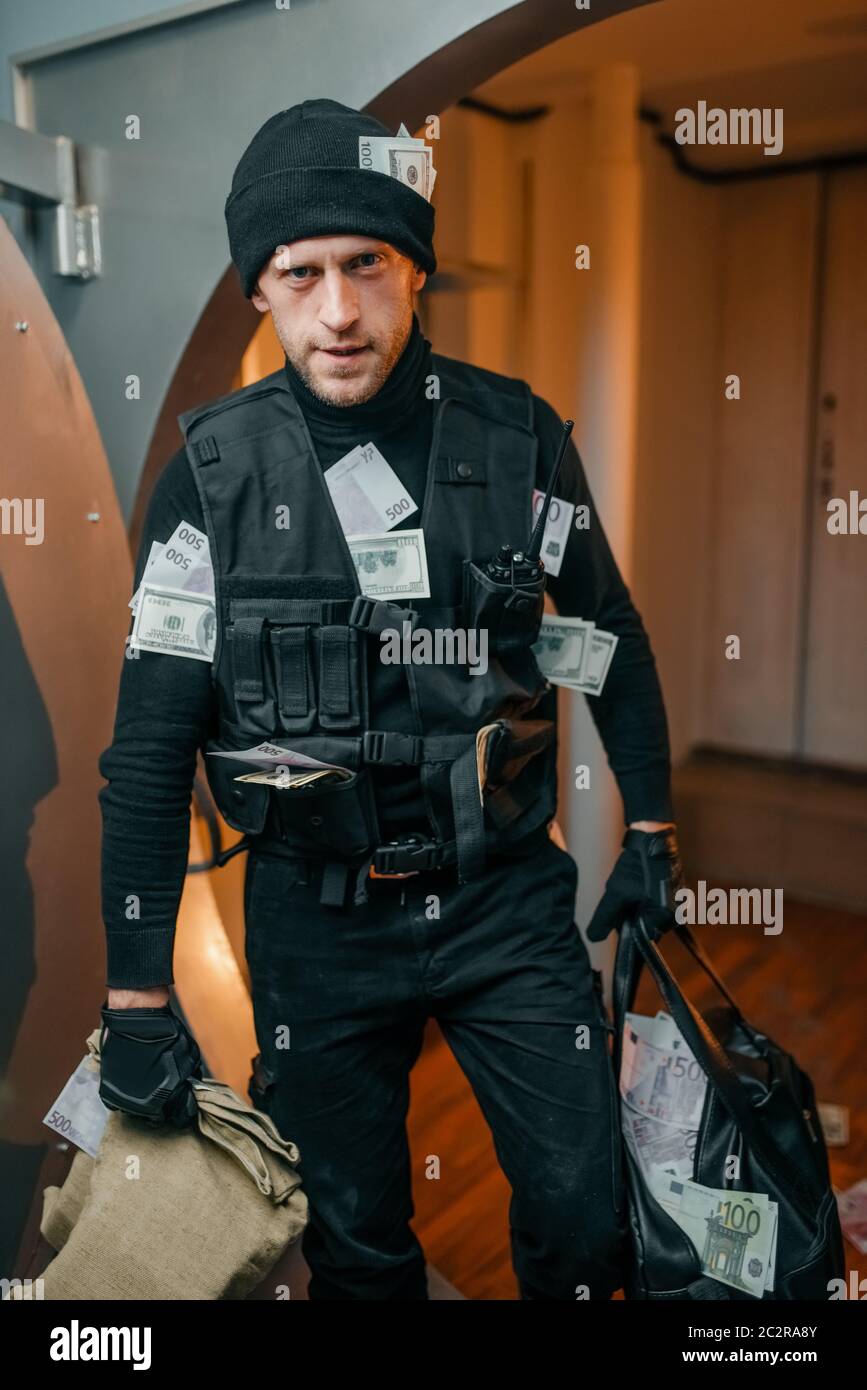 Bank robbery, male robber in black uniform holds bags full of money ...