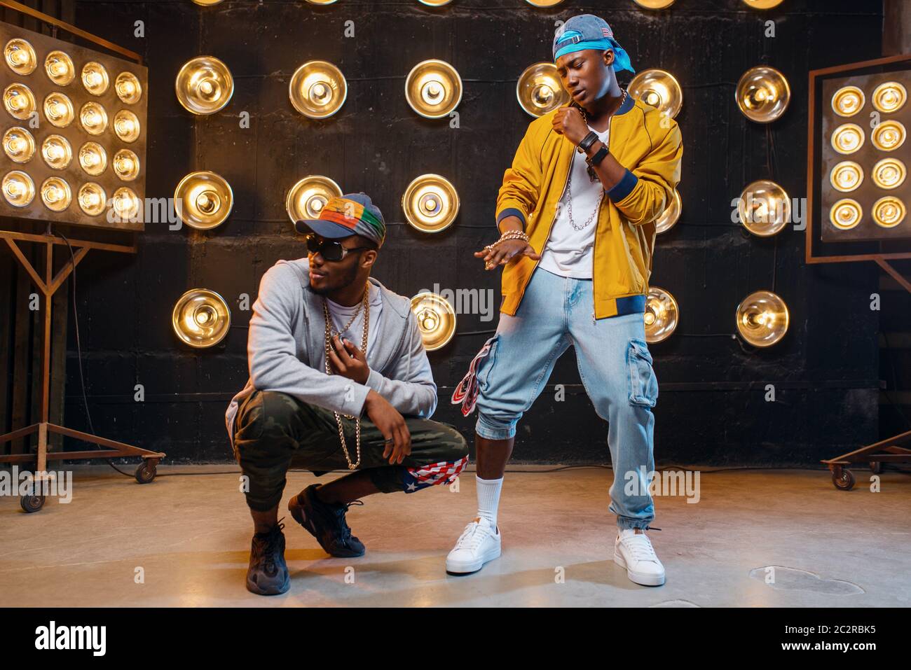 Black rappers in caps dance on stage with spotlights on background. Rap ...