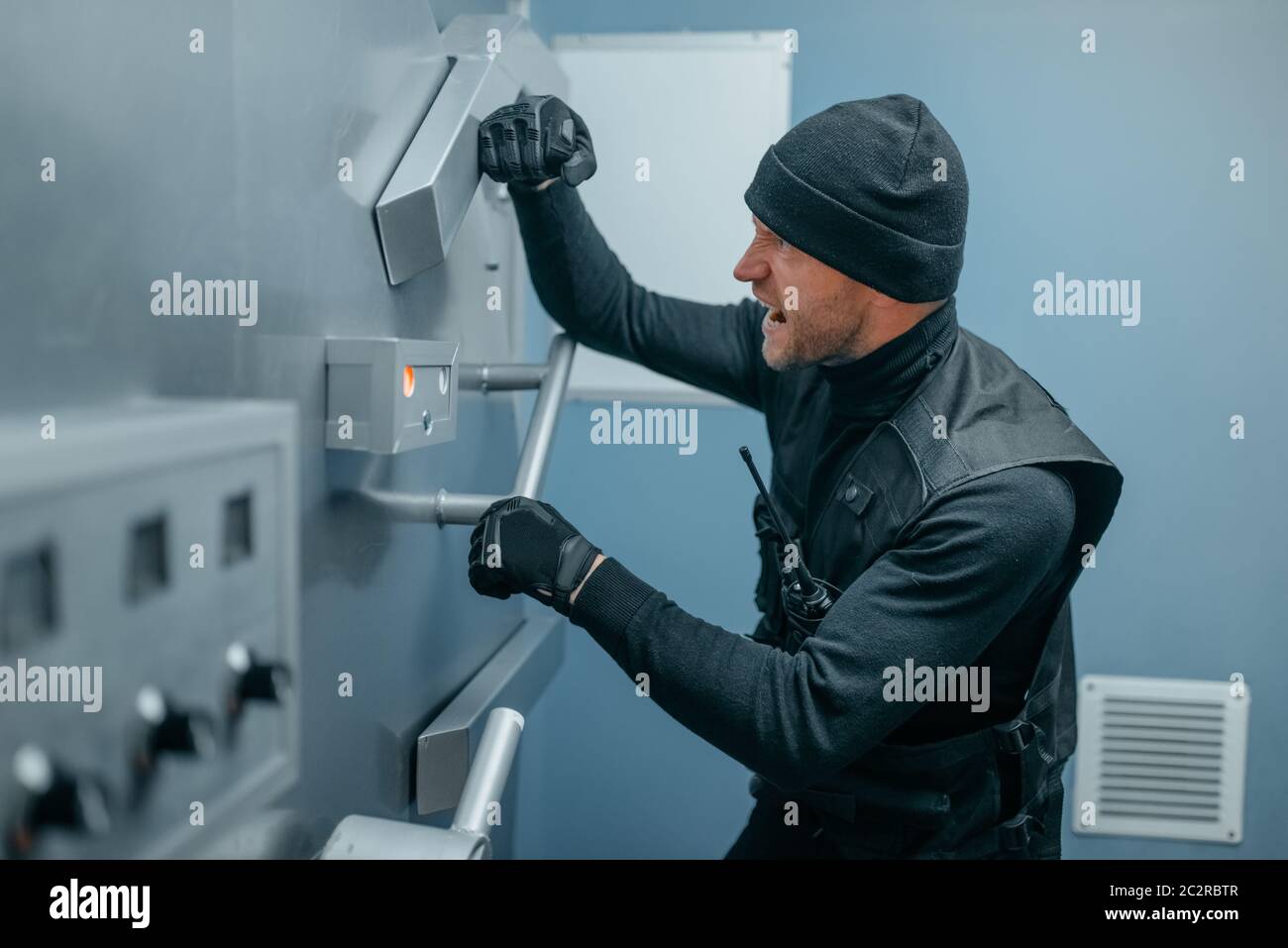 Bank robbery, male robber in black uniform trying to open vault lock ...