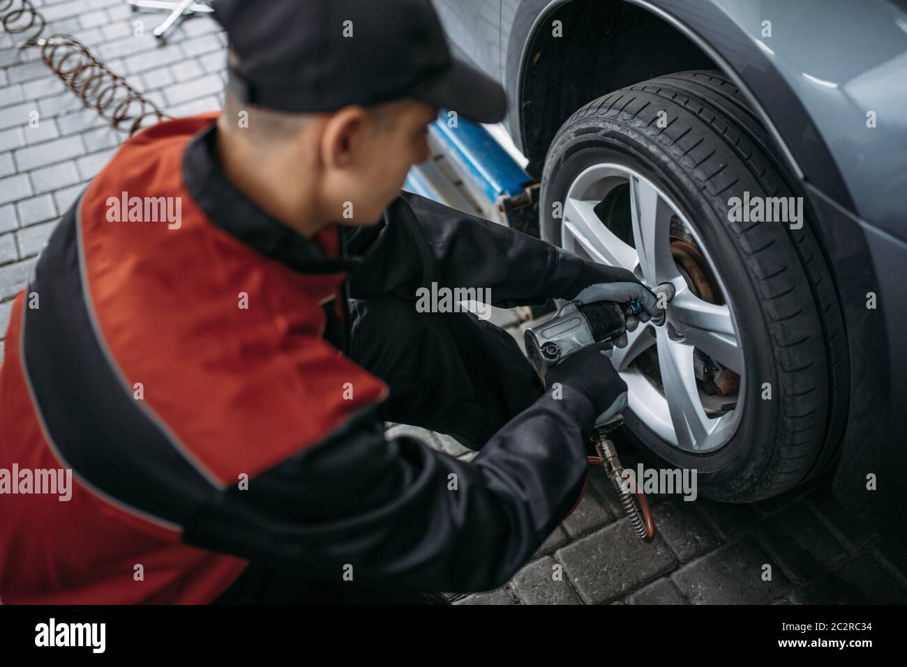 Mechanic with pneumatic wrench unscrews the wheel in tire service. Man ...