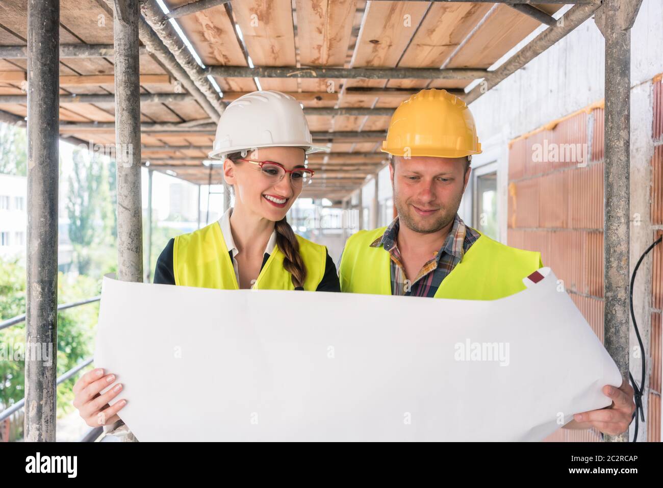 Construction worker and builder on scaffolding reading the plan in ...