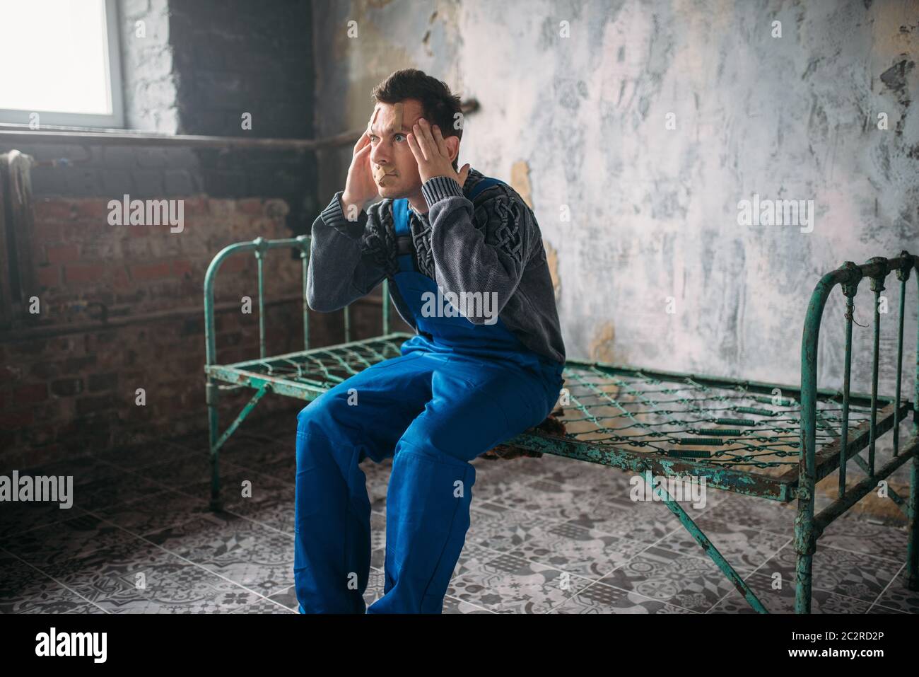 Disturbed madman sitting on a rusty bed, face sealed with plaster ...