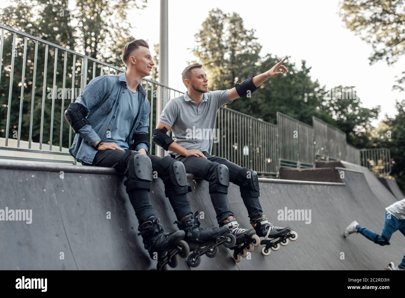 Roller skating, two male skaters sitting on the ramp in park. Urban ...