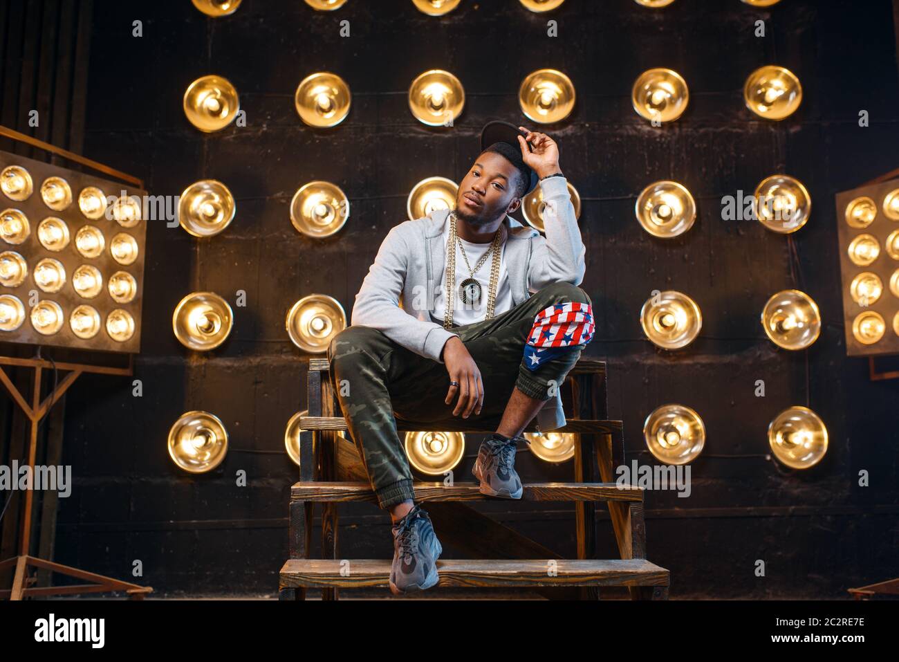 Black rapper in cap poses, perfomance on stage with spotlights on ...