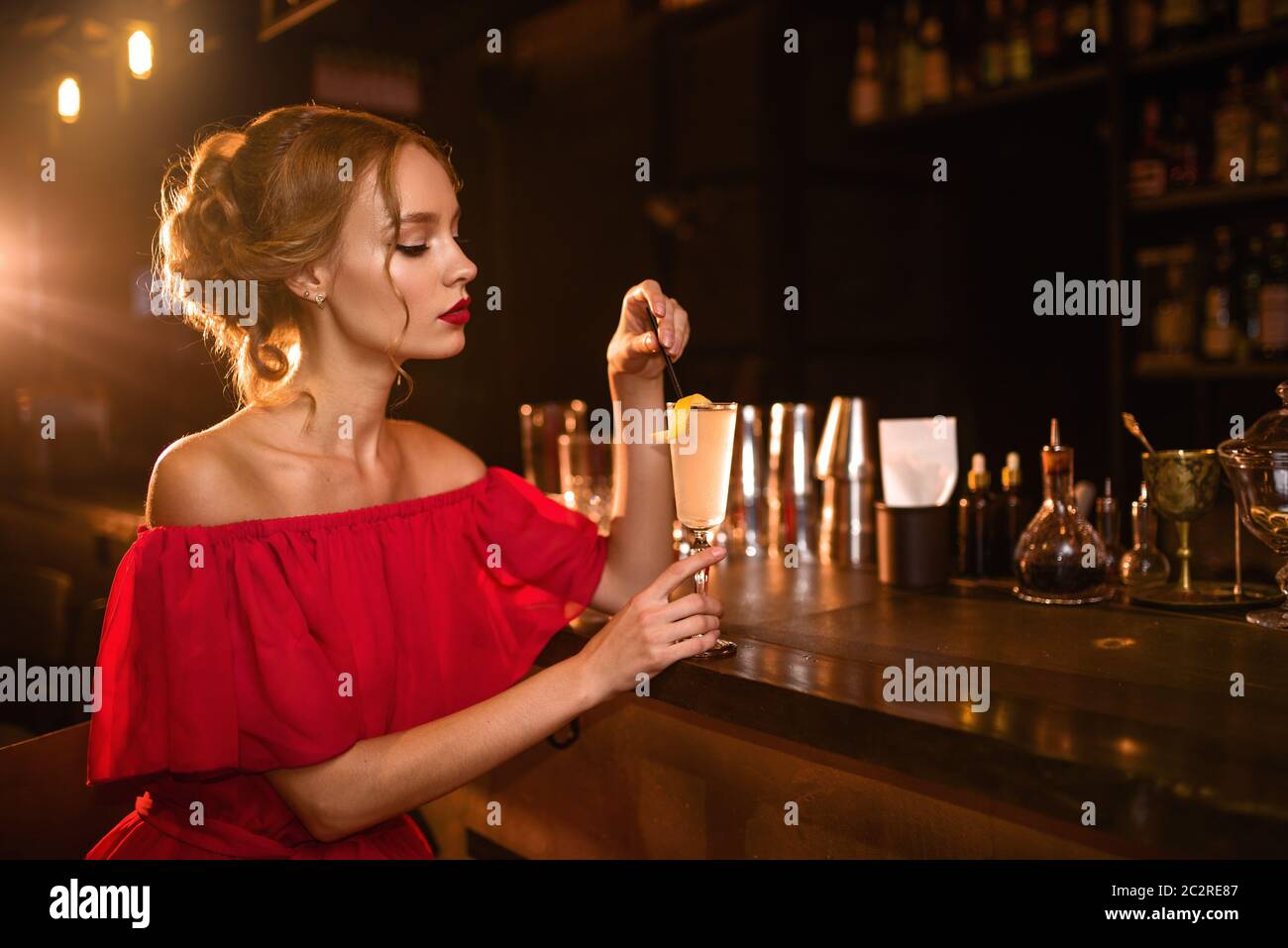 Beautiful woman in red dress drinks alcohol cocktail at the bar counter ...