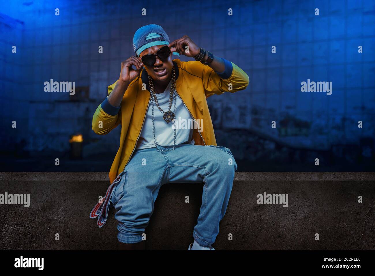 Black rapper in cap and sunglasses poses in underpass, singer in grunge ...