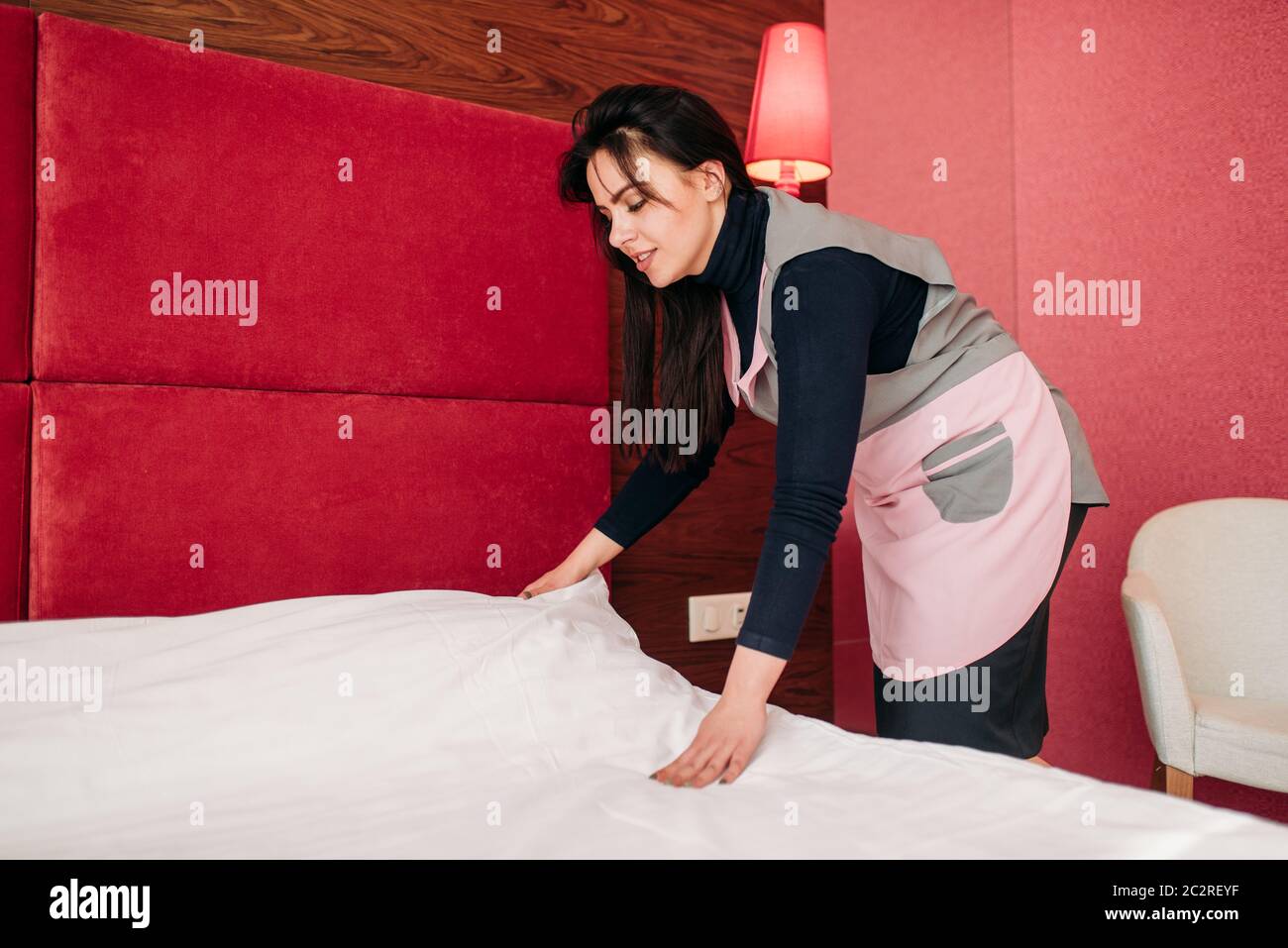 Pretty maid in uniform makes the bed in the hotel room. Cleaning ...