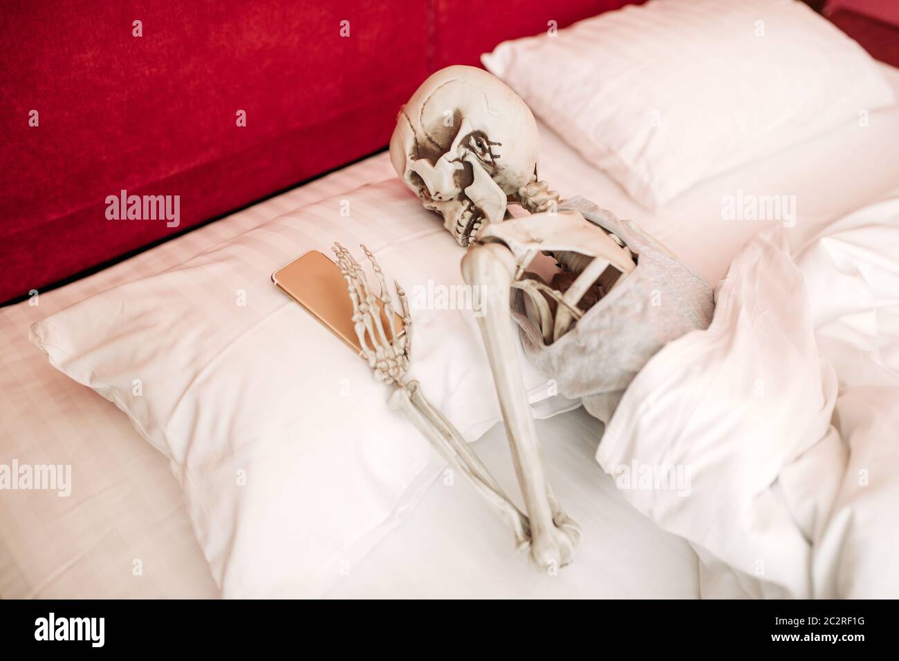 Human skeleton with mobile phone in hand lies in bed, black humor ...