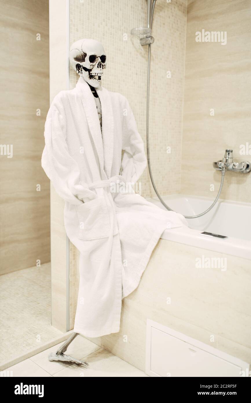 Human skeleton in white bathrobe sitting on the edge of the bath in ...