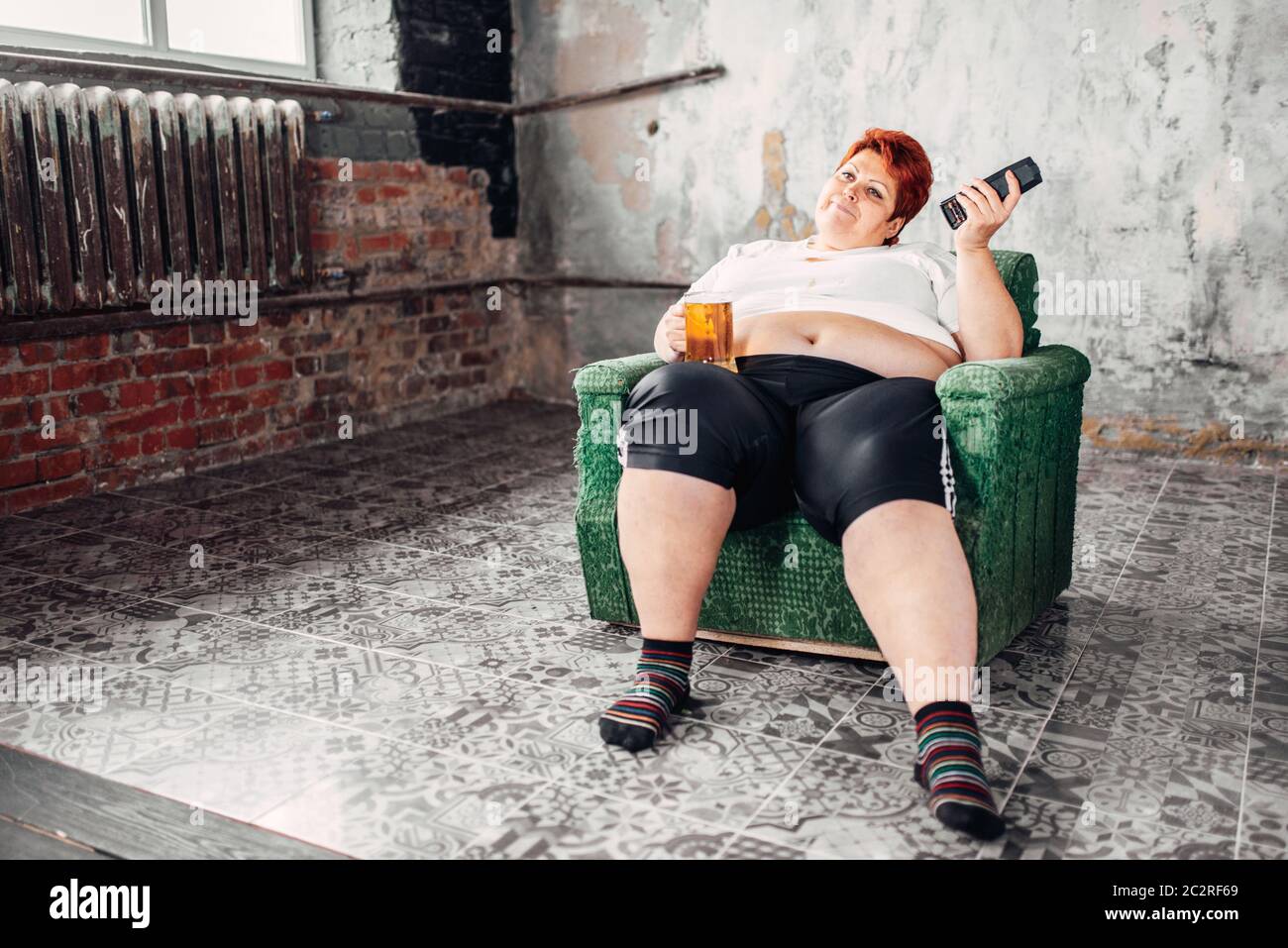 Overweight woman sitting in chair and drinks beer, high calorie food ...