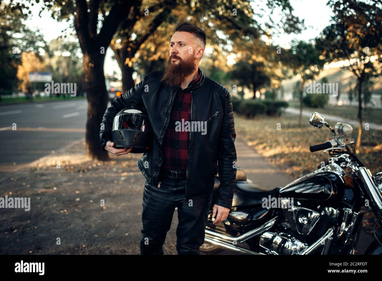 Biker in leather jacket standing near black chopper. Vintage bike ...