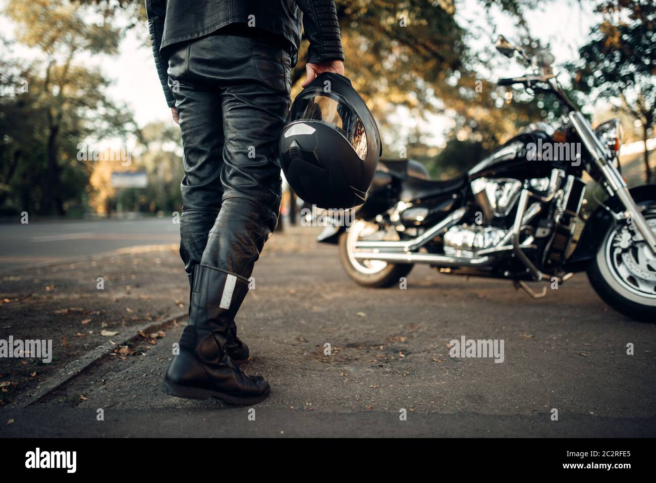 Motorcyclist with helmet in hand goes to his chopper, back view ...