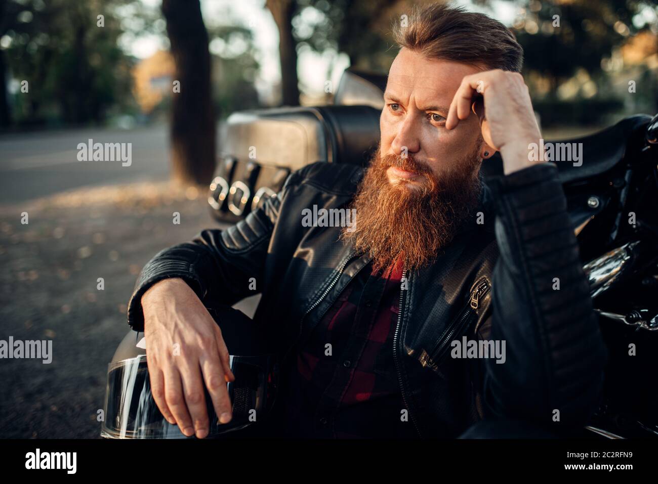 Biker with helmet in hands sitting on the ground against his chopper ...
