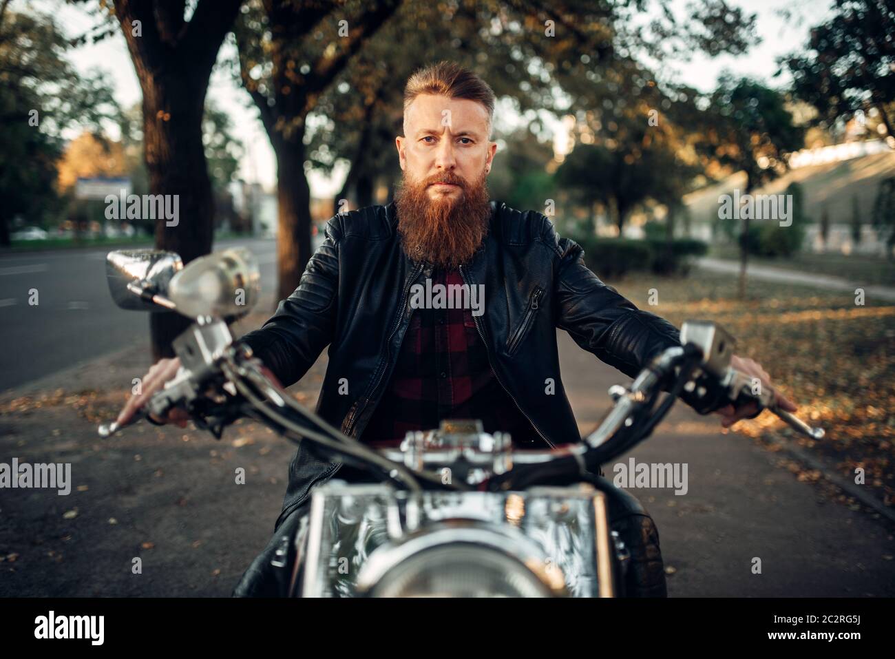 Bearded motorcyclist in leather jacket sitting on classical chopper ...