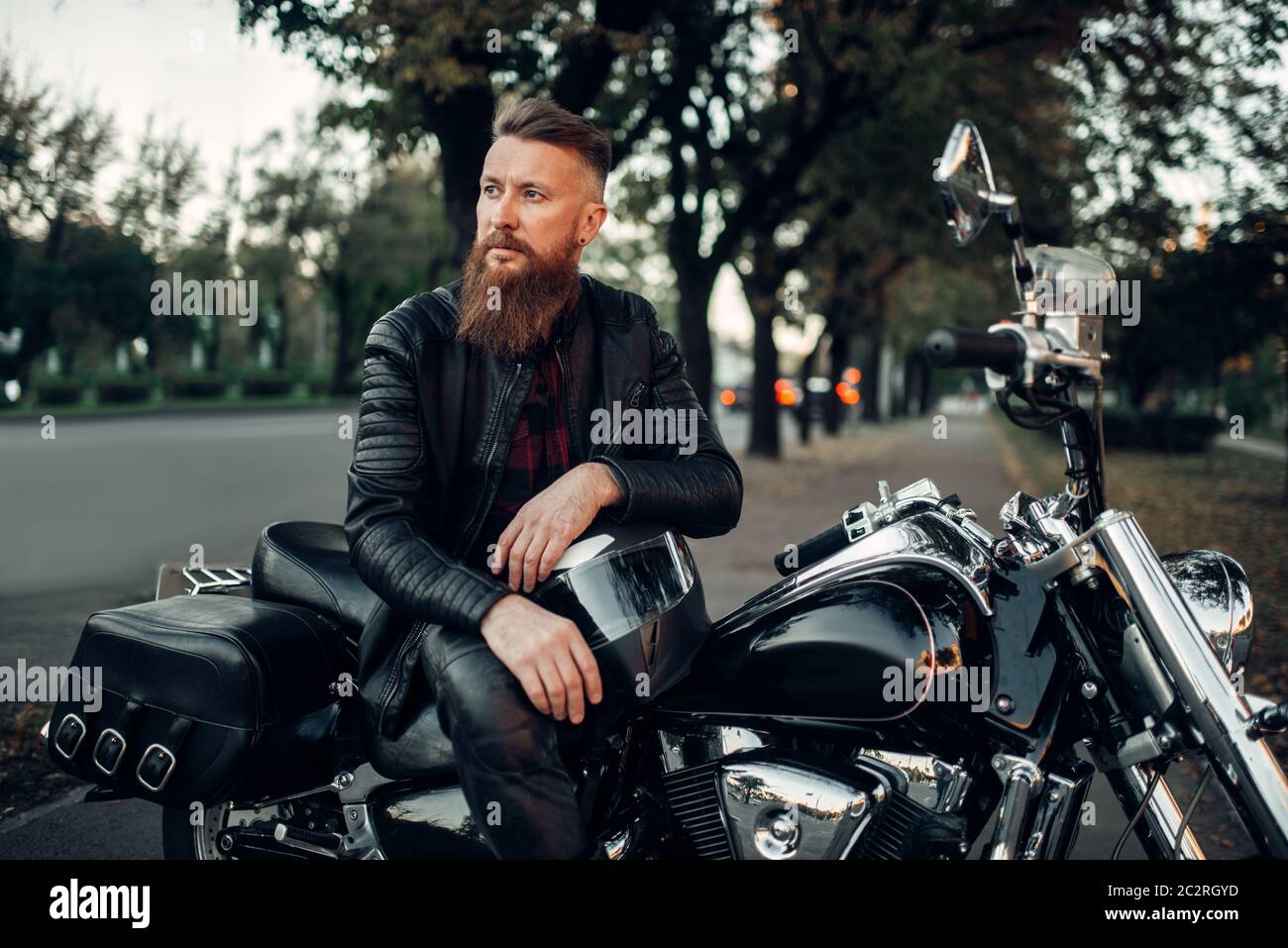 Baerded biker poses on chopper leaning on a helmet. Vintage bike, rider ...