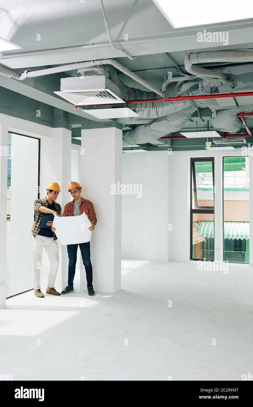 Two modern construction engineers standing together in unfinished room ...