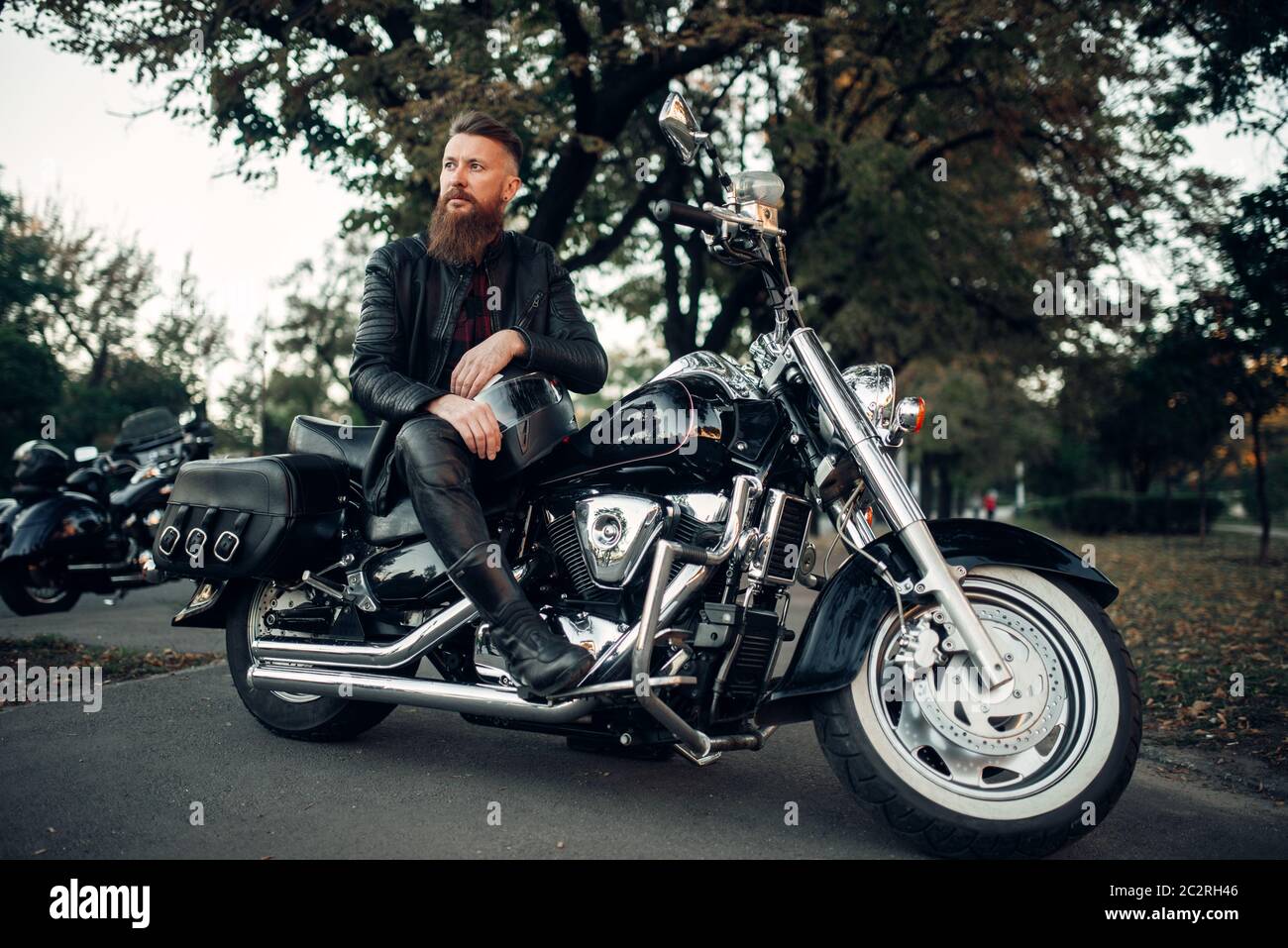 Baerded biker poses on chopper leaning on a helmet. Vintage bike, rider ...
