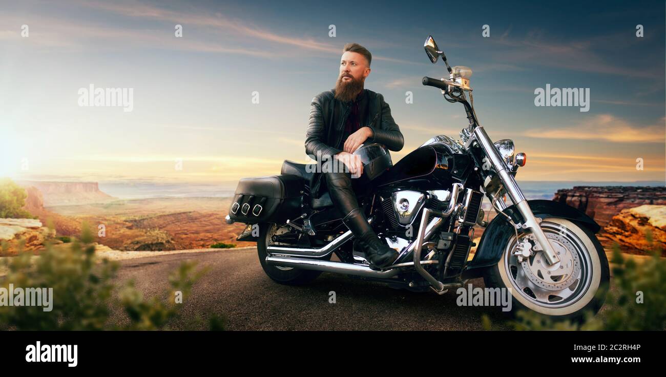 Biker sitting on his chopper and looks on sunset in desert valley ...