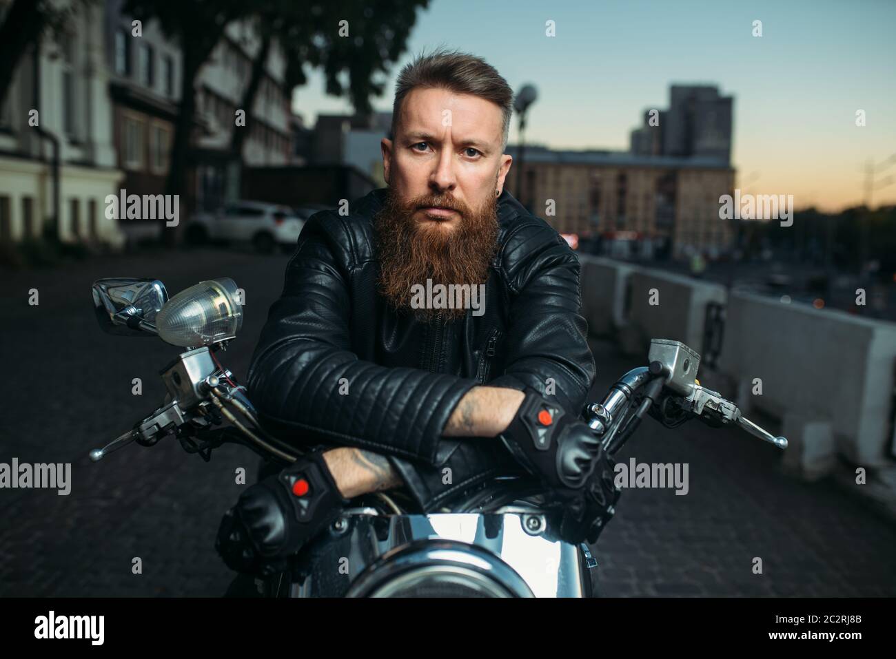Brutal bearded biker poses on chopper in city, front view. Vintage bike ...