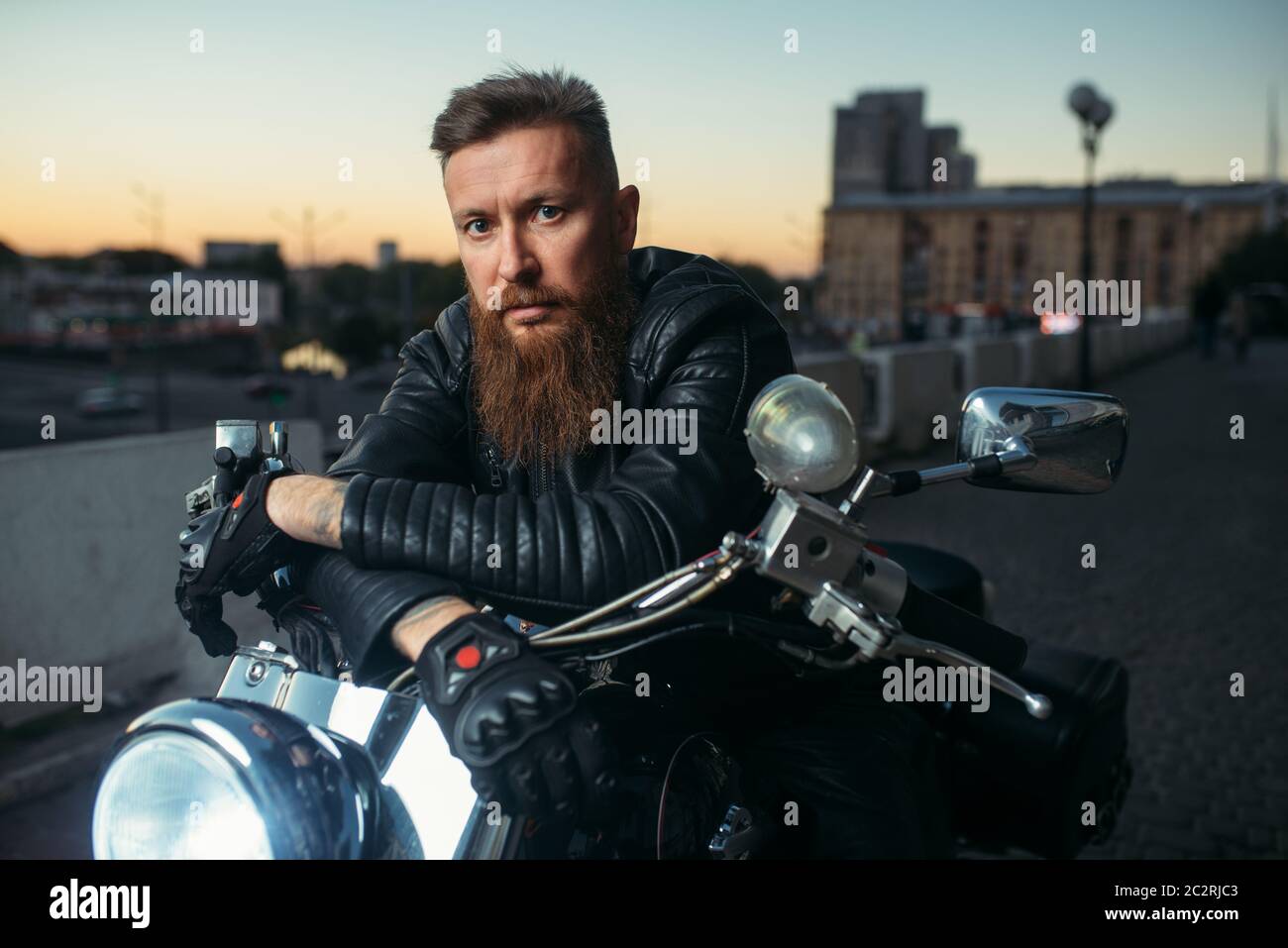 Brutal bearded biker poses on chopper in city, front view. Vintage bike ...