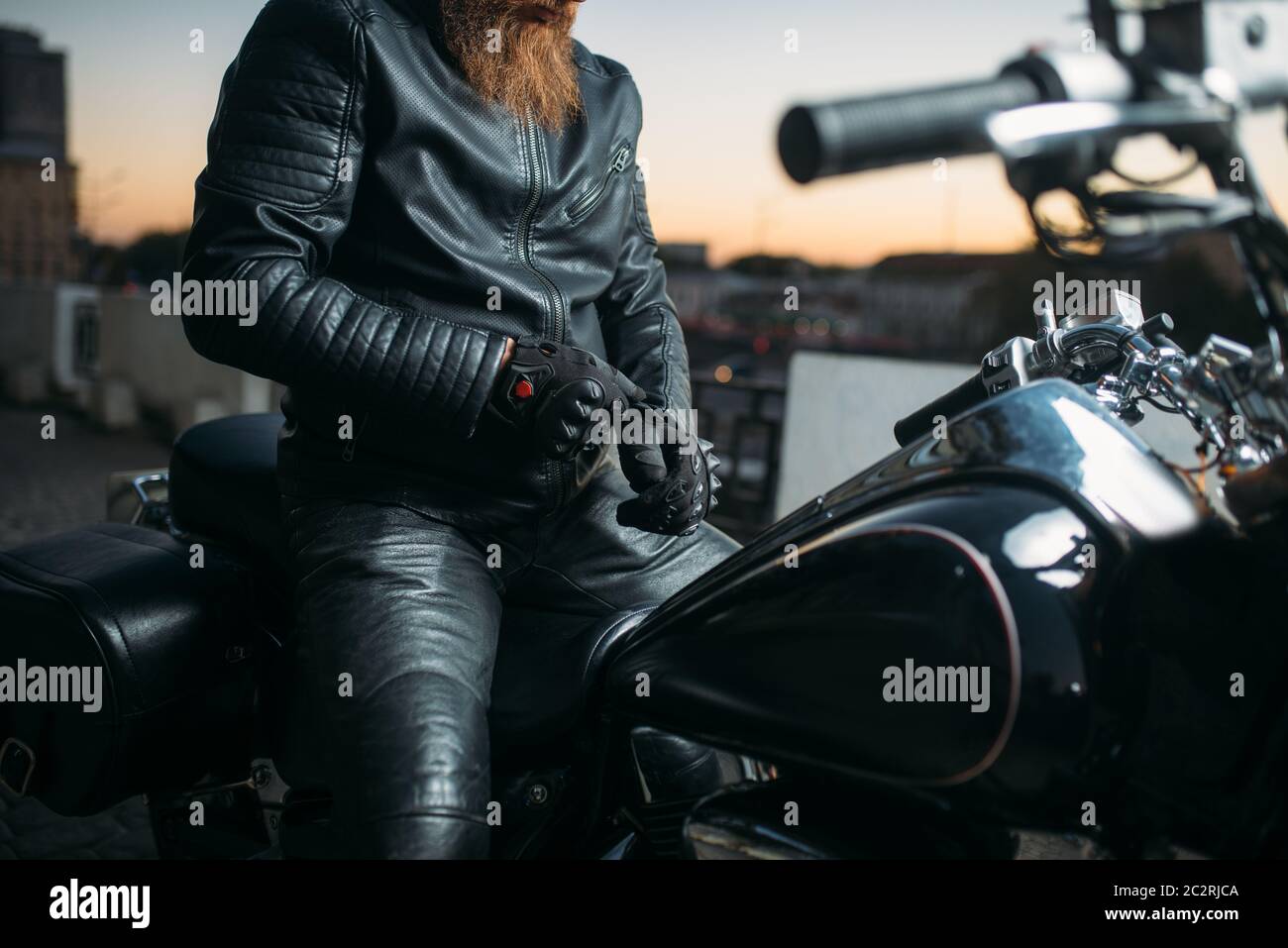 Biker poses on a motorcycle in city on sunset, classical chopper ...
