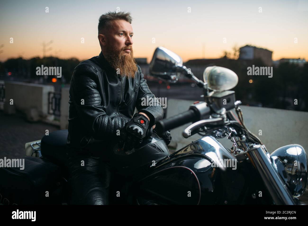 Biker poses on a motorcycle in city on sunset, classical chopper ...