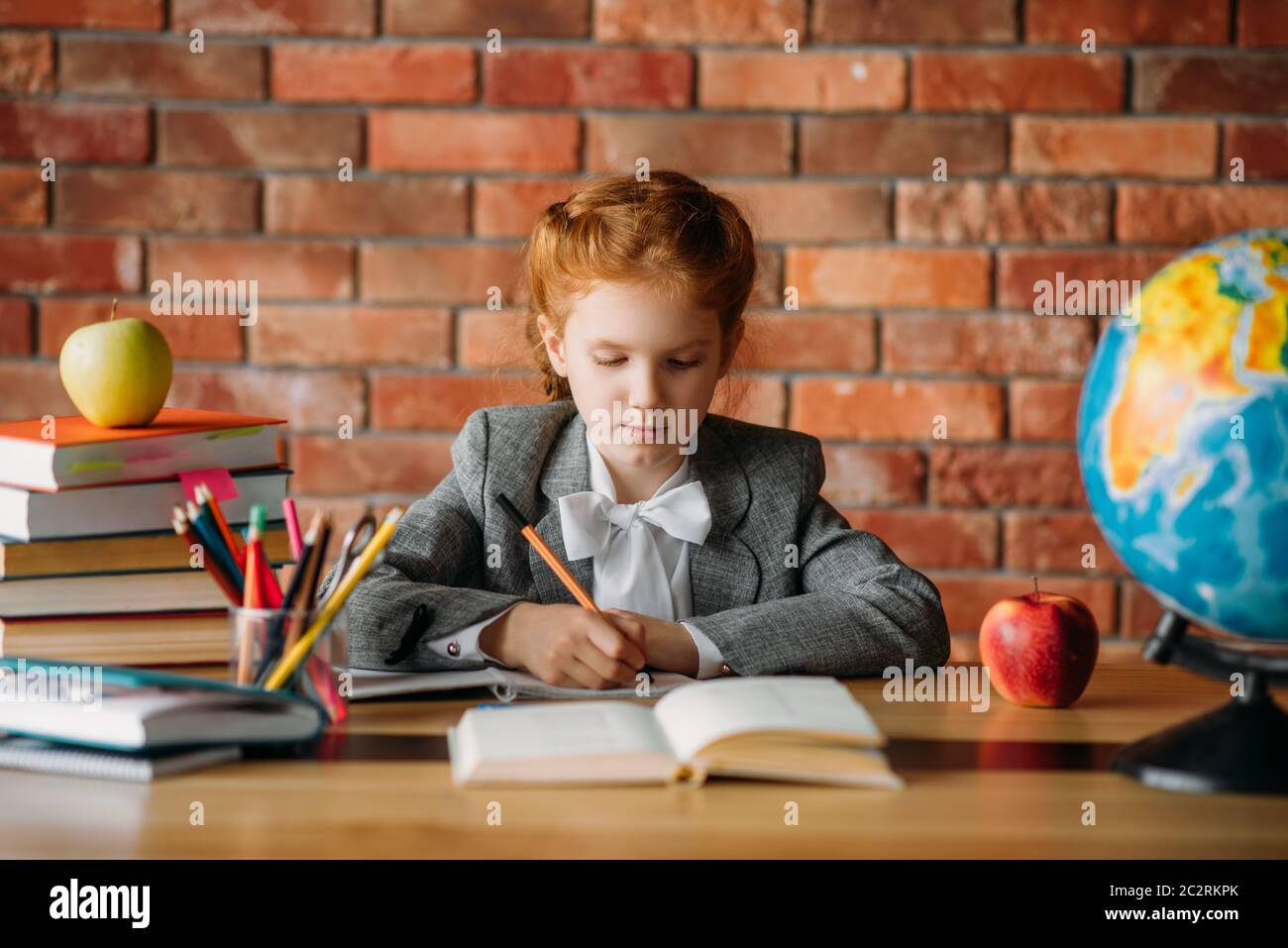 Cute schoolgirl doing homework at the table with textbooks, apples and ...