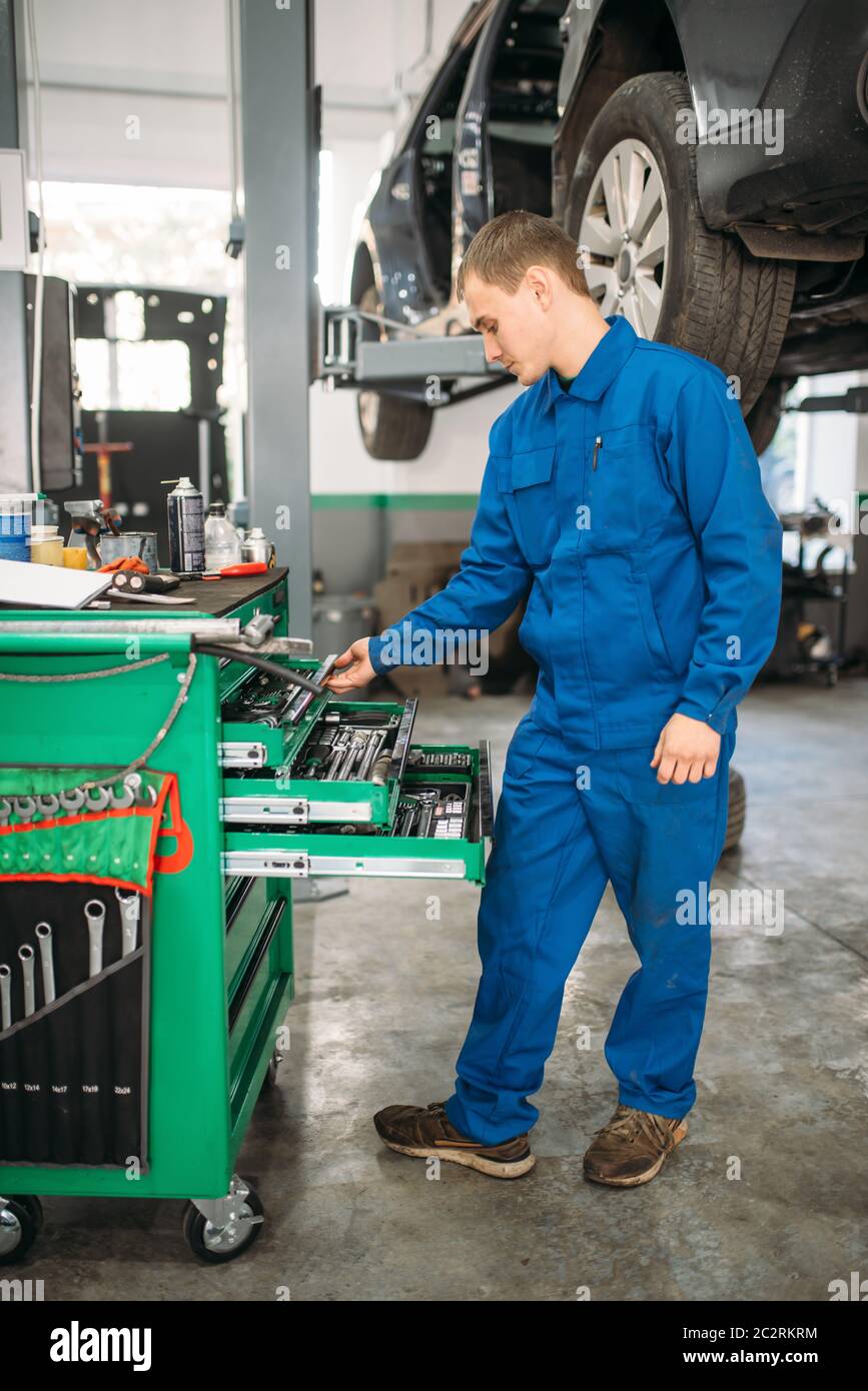 Repairman reaching for the wrench in tool box, car on the lift on ...