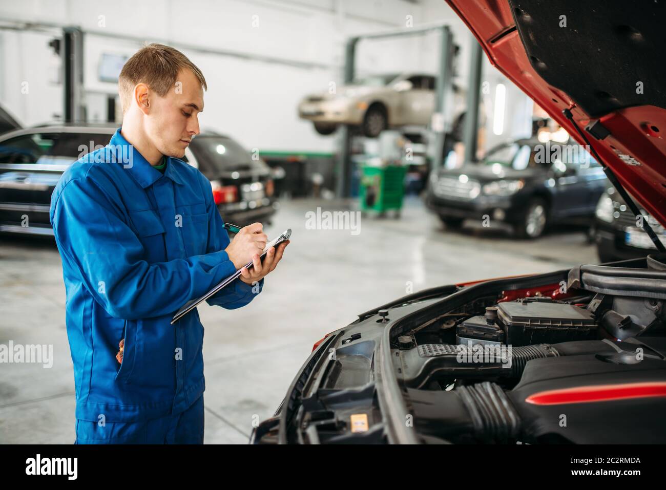 Technician with notebook fills the check list, car with opened hood ...